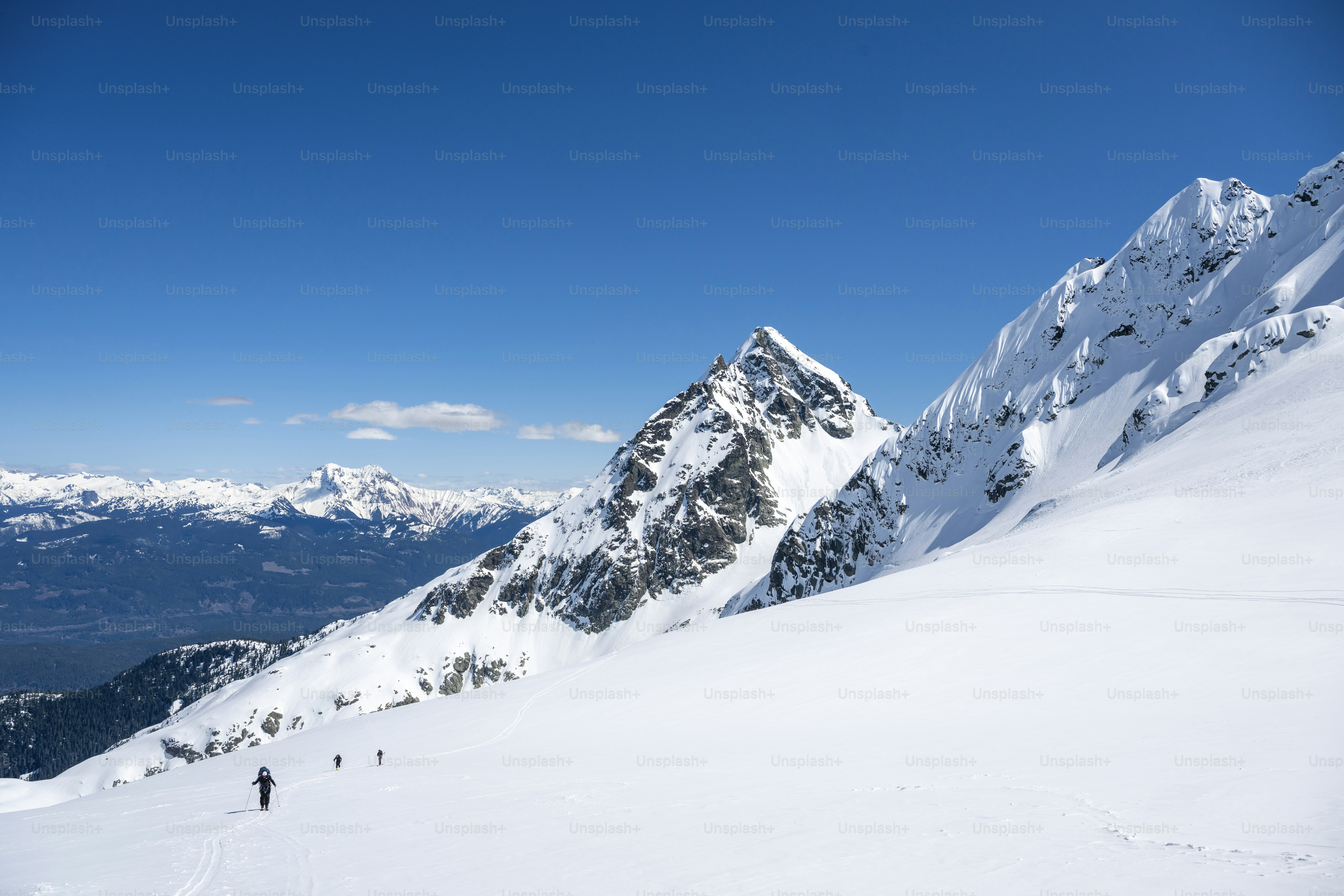 Group of backcountry skiers climb mountain above snowcapped peaks ...