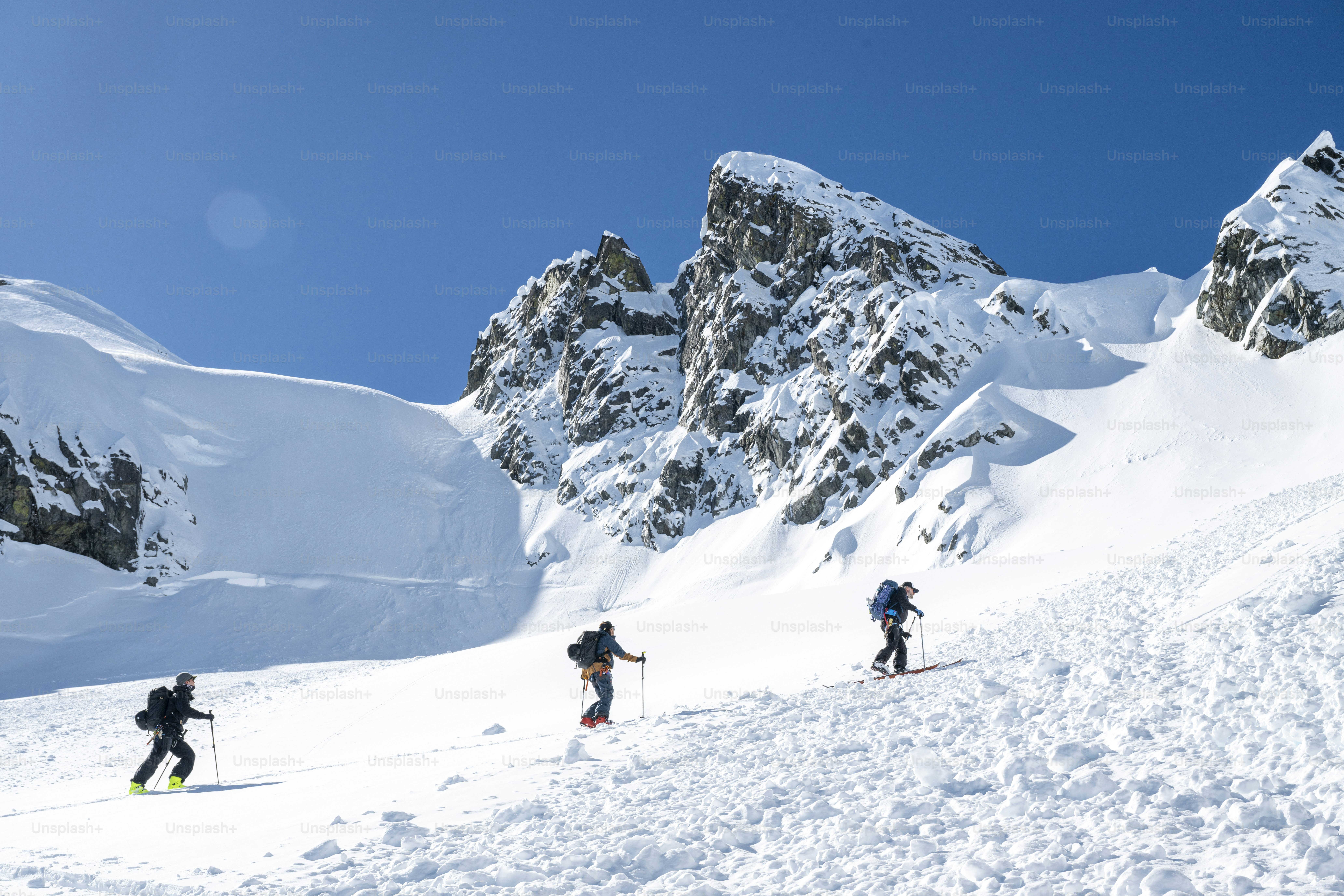 Group of backcountry skiers climb mountain above snowcapped peaks ...