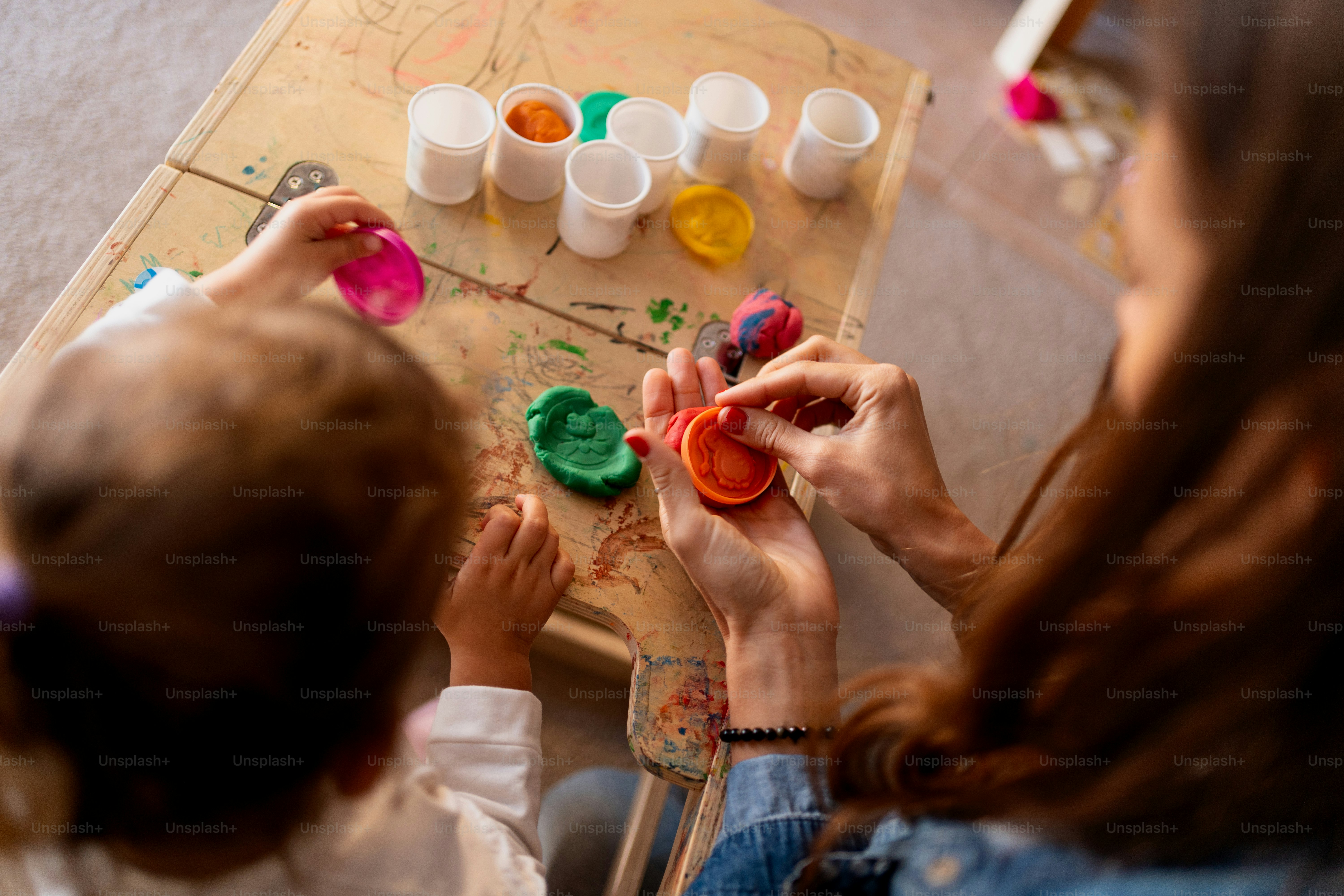 Teacher and little girl playing with modeling clay in kindergarten ...
