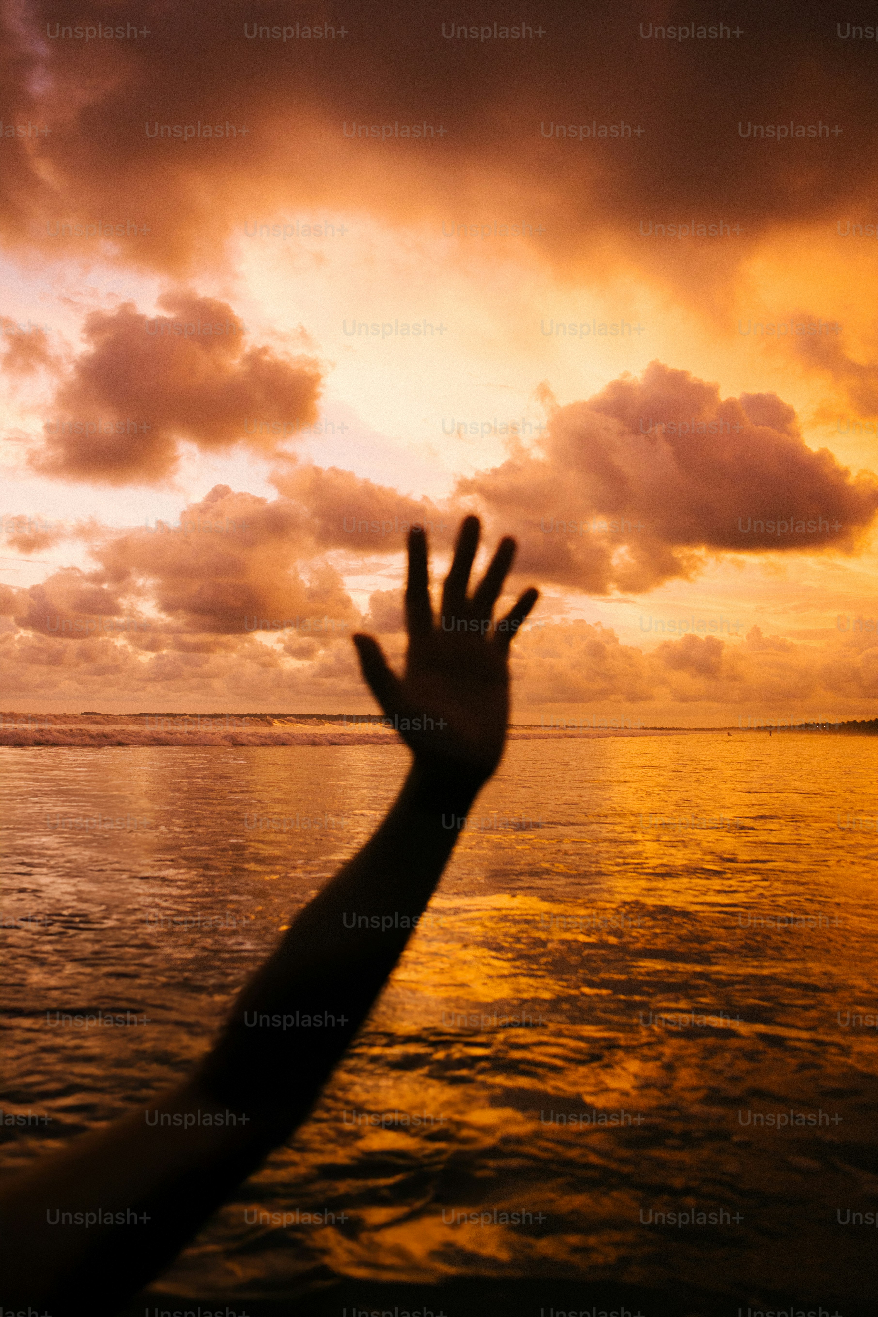 Mano agitando la mano en la dramática puesta de sol sobre las olas del ...