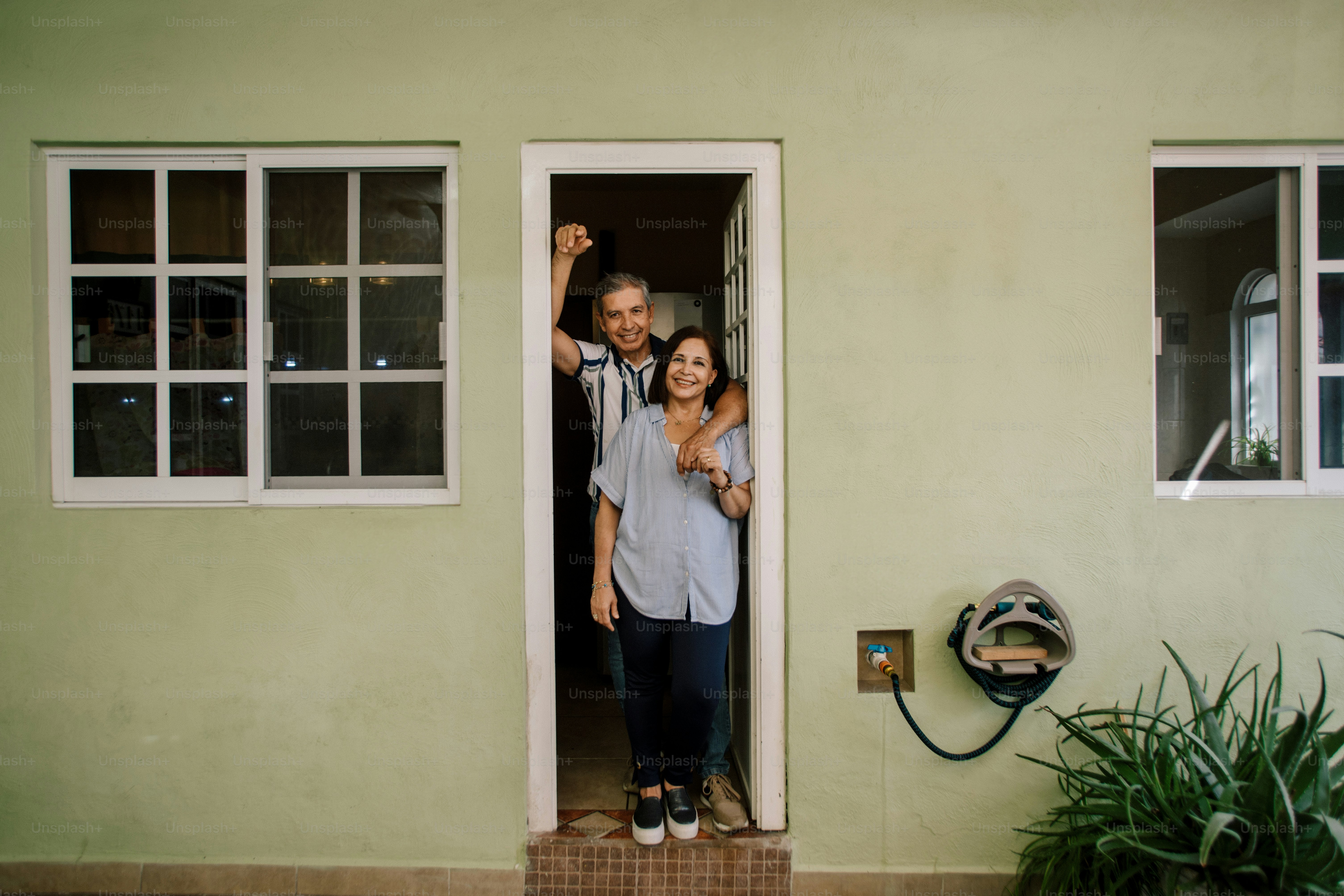 Couple standing in a doorway of a light green house. photo – Portrait ...