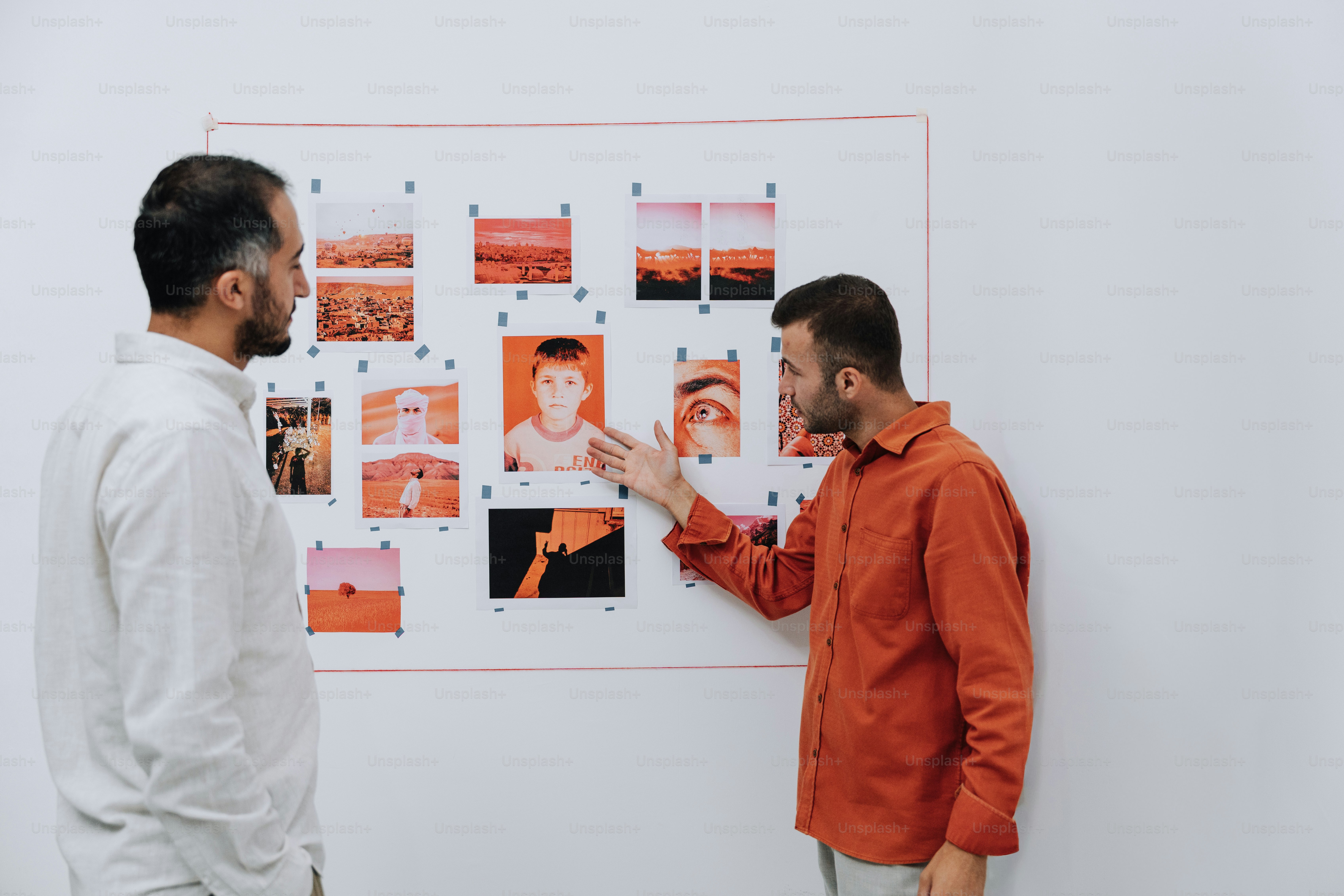 Two men discussing photographs on a wall. photo – Art Image on Unsplash