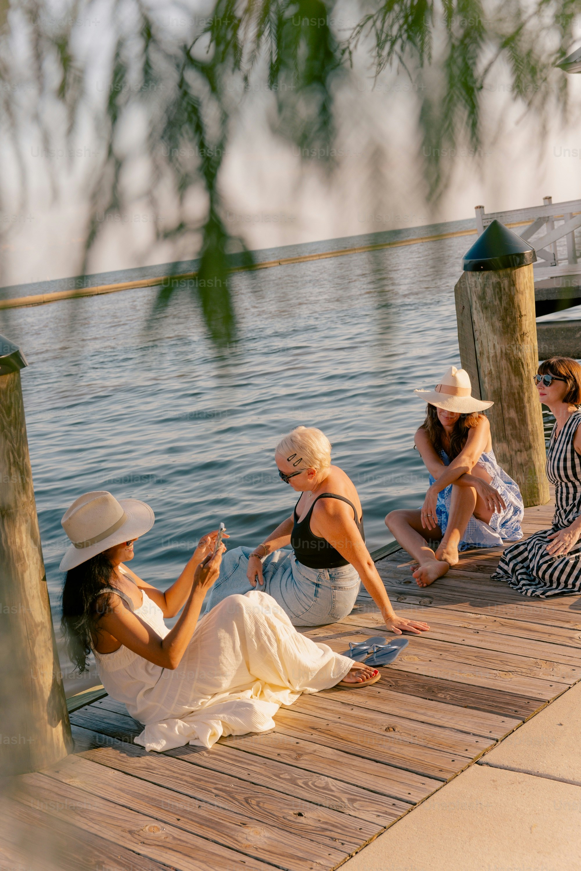 Four women in hats relax on a wooden dock. photo – Sunset Image on Unsplash