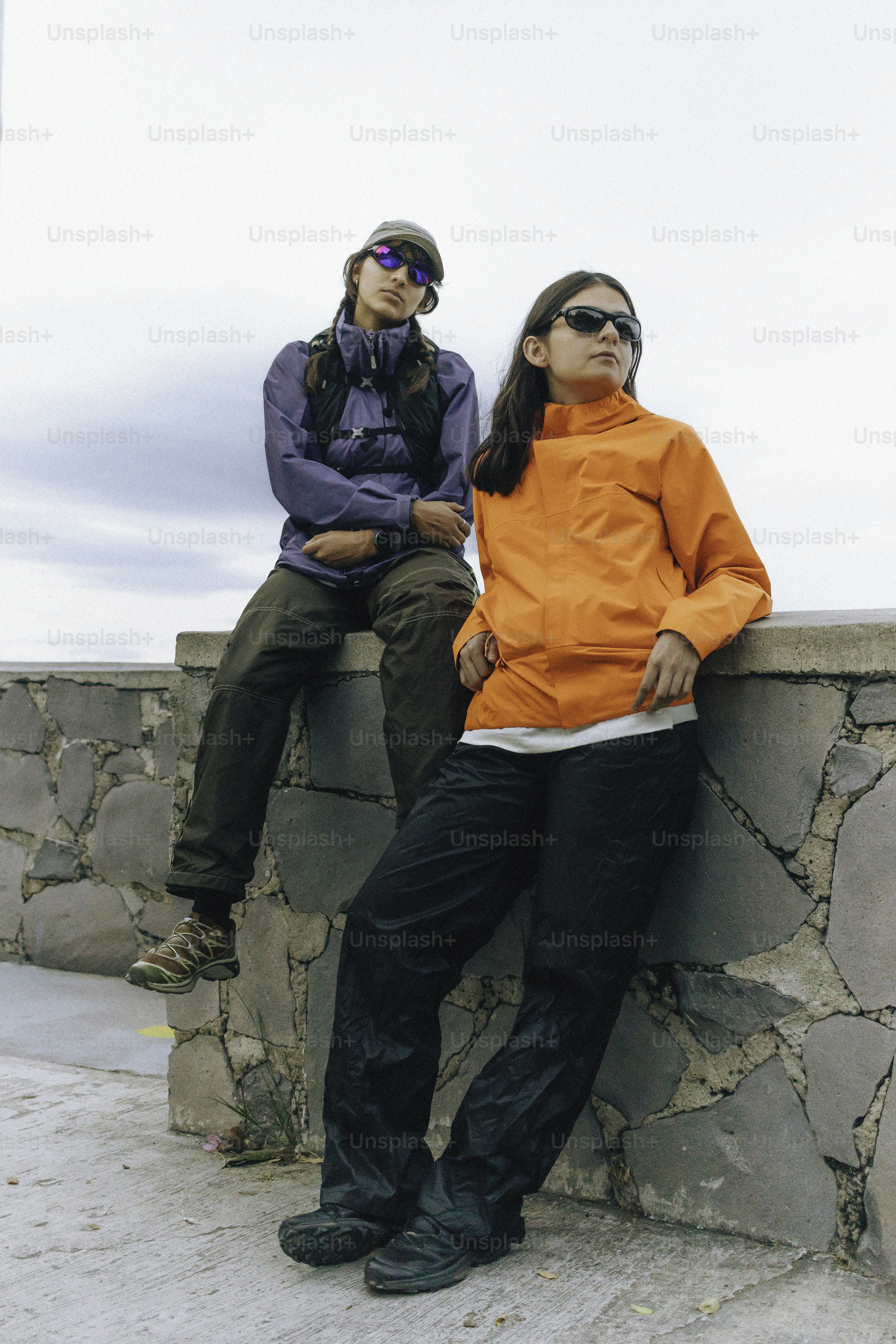 Two people in outdoor gear posing by stone wall. photo – Fashion Image ...