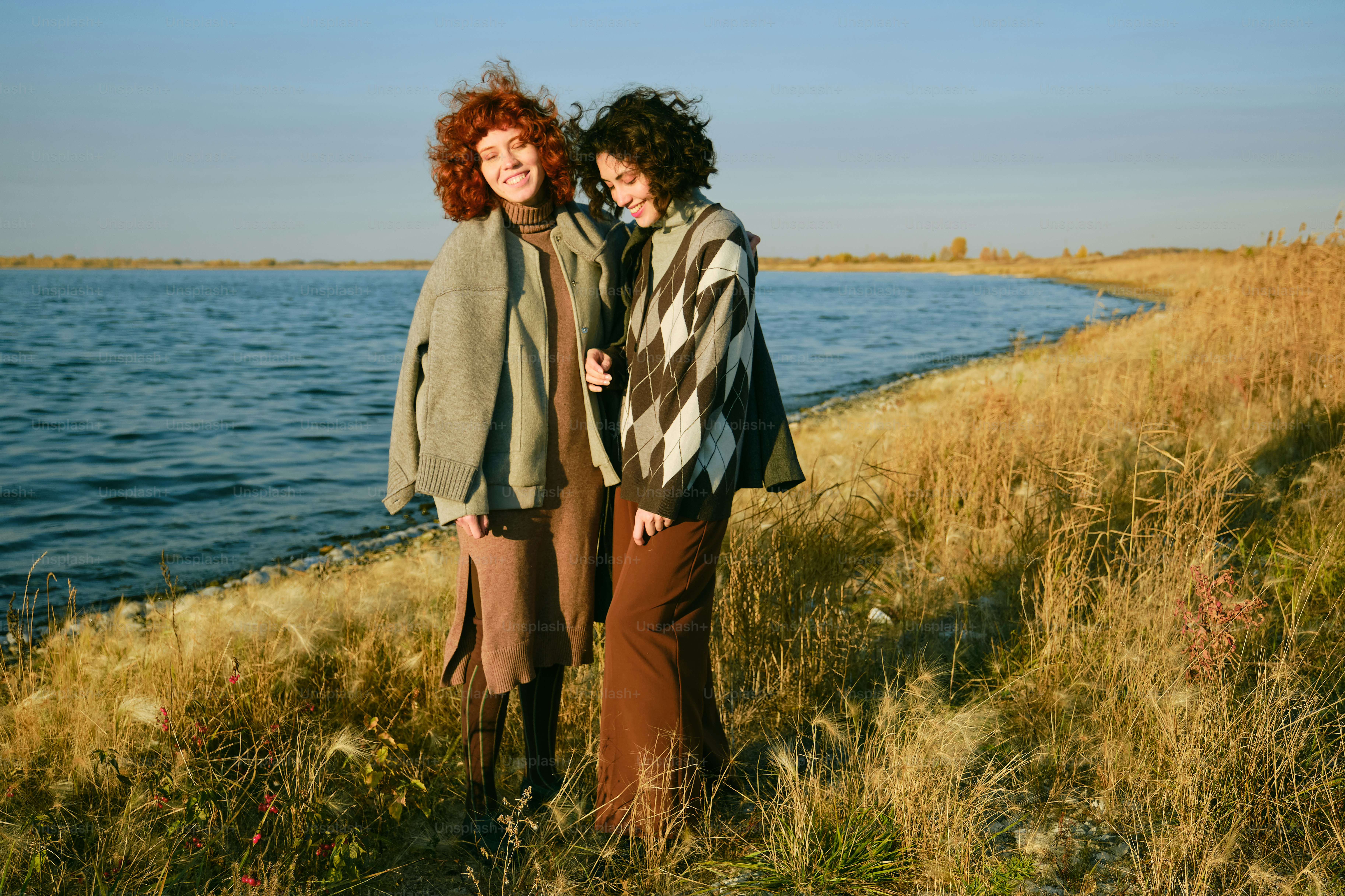 Two women stand on a rocky shore near water photo – Fashion Image on ...