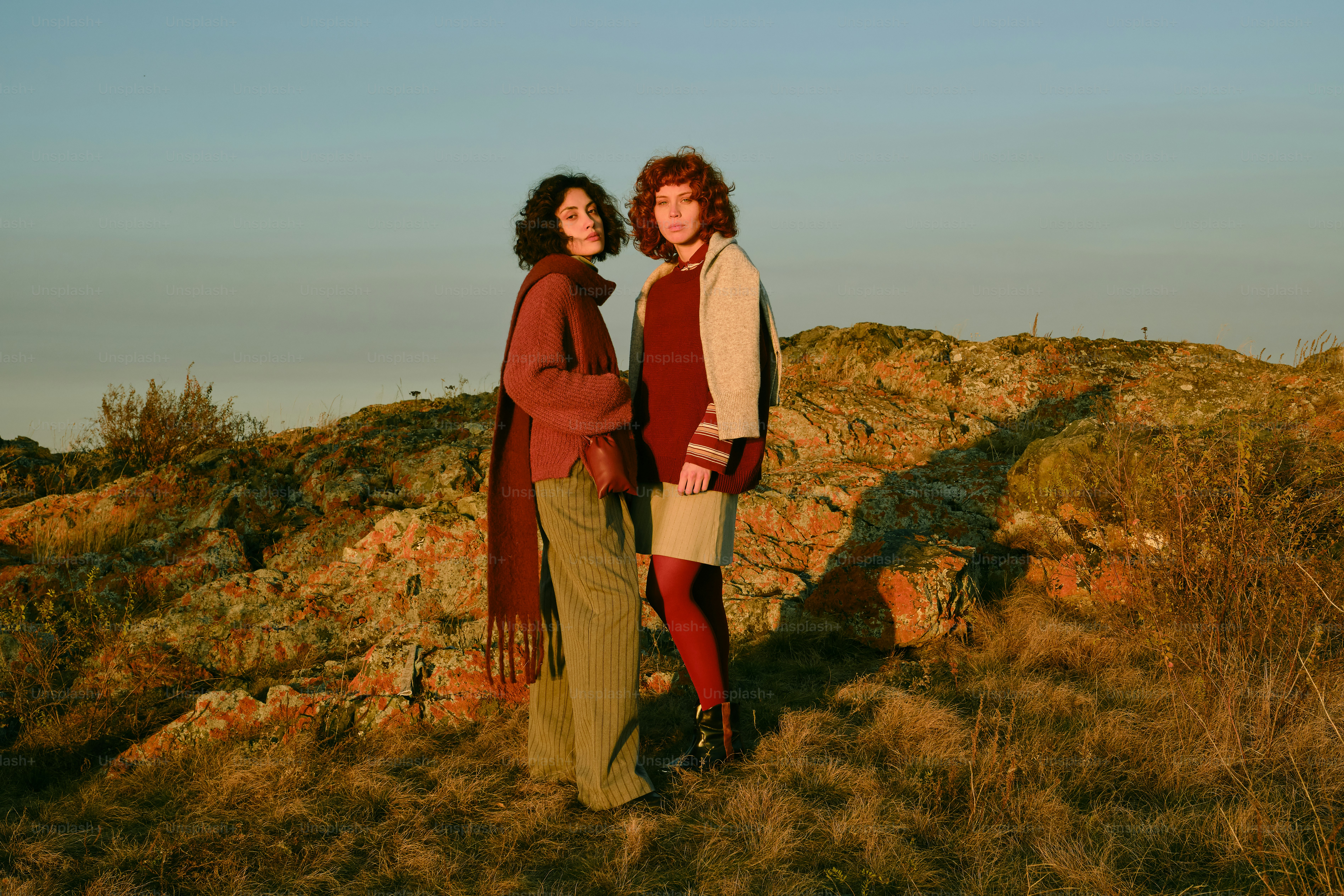 Two women stand on a rocky shore near water photo – Fashion Image on ...
