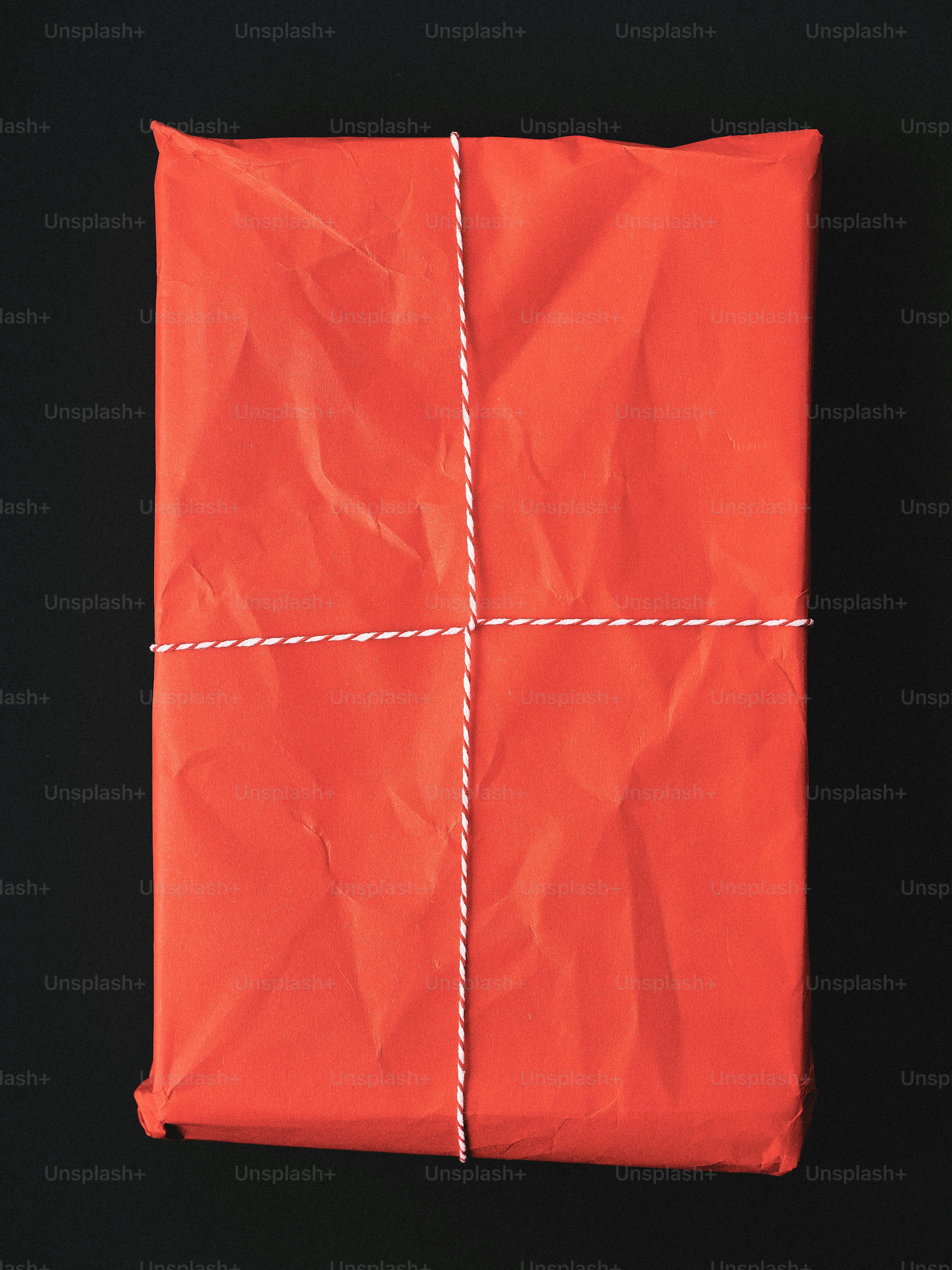 A gift wrapped in red paper with white string. photo – Book Image on ...