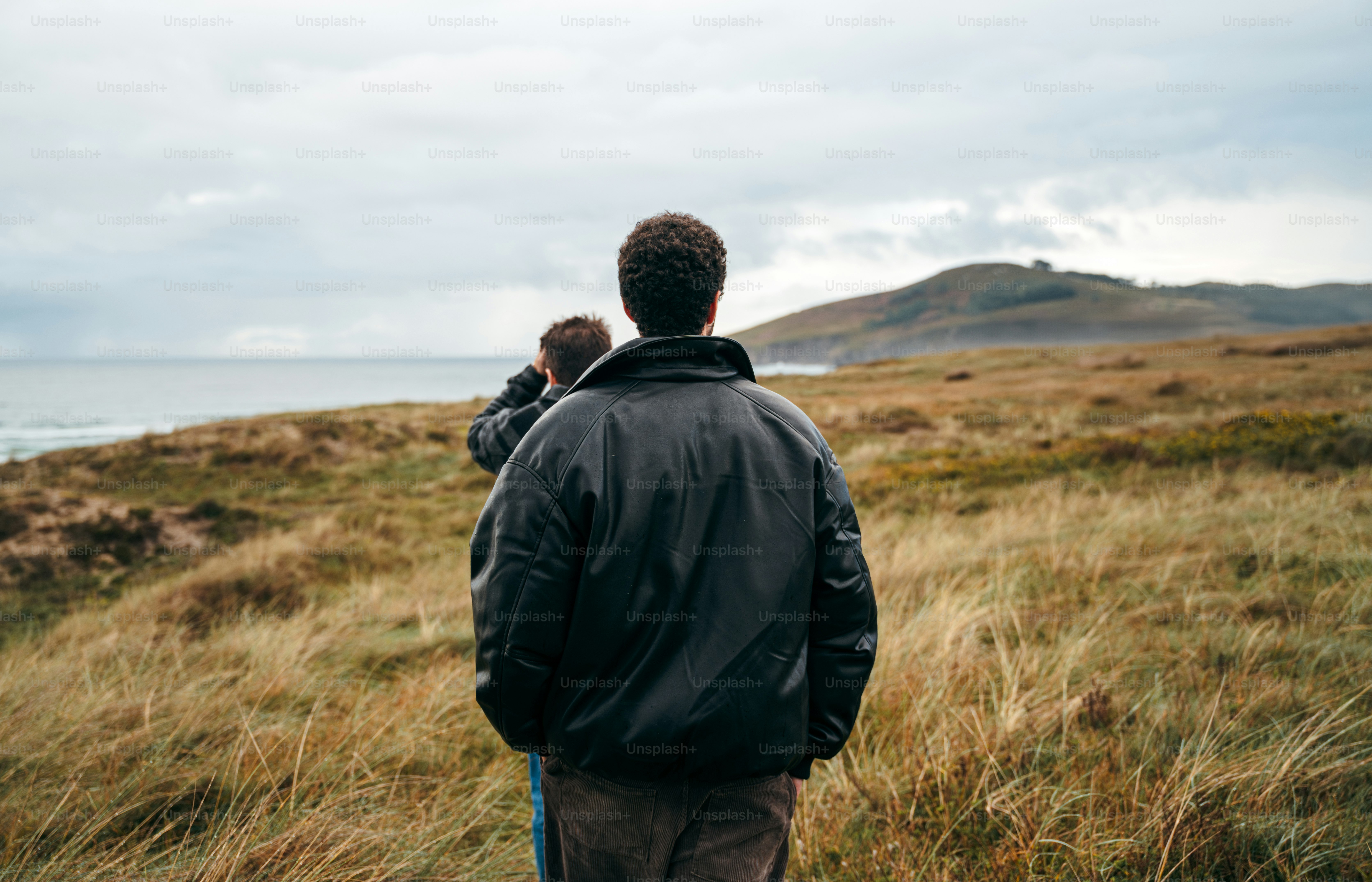 Two men standing by a yellow structure near the ocean. photo – Autumn ...