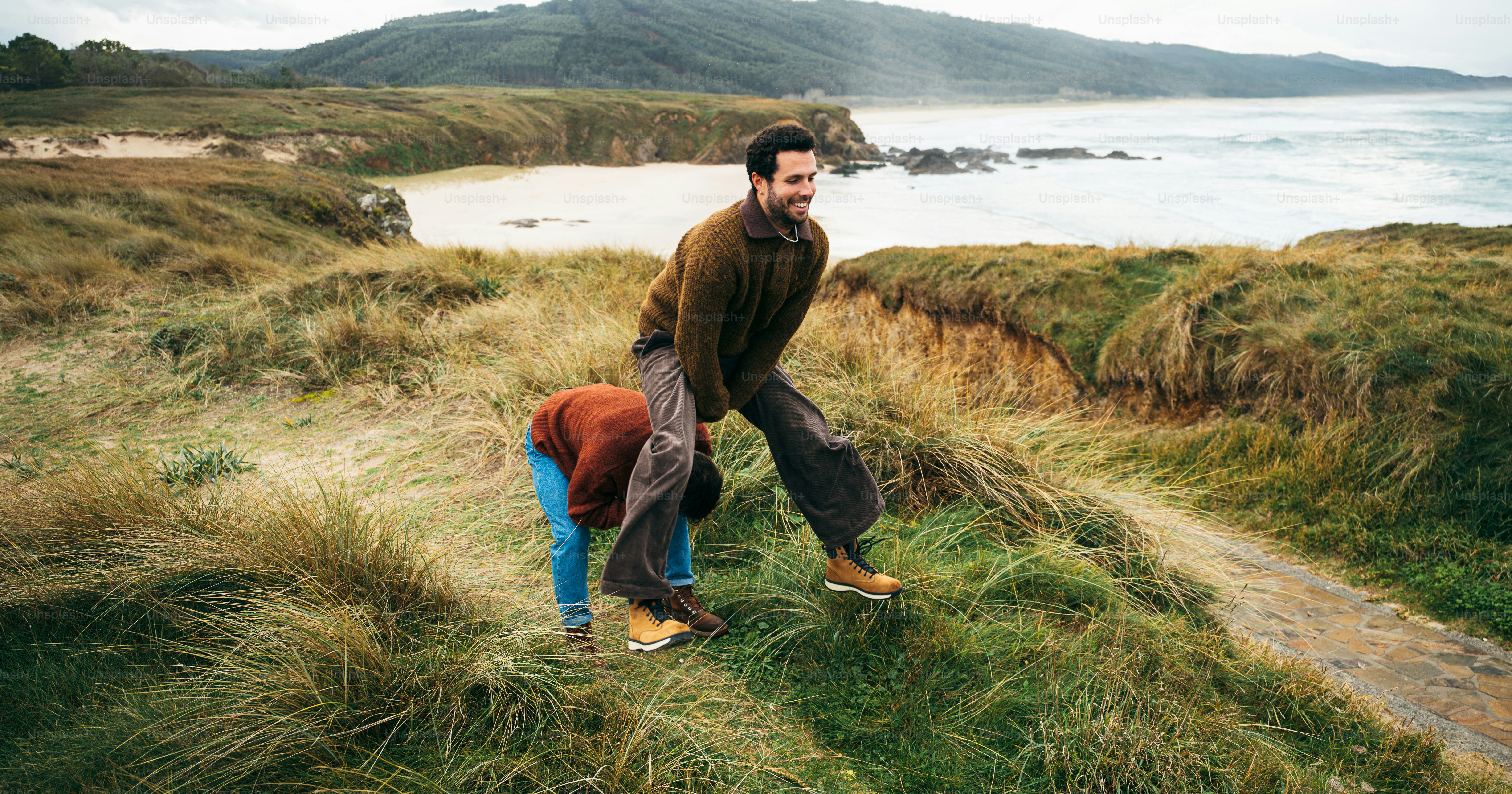 Two men standing by a yellow structure near the ocean. photo – Autumn ...
