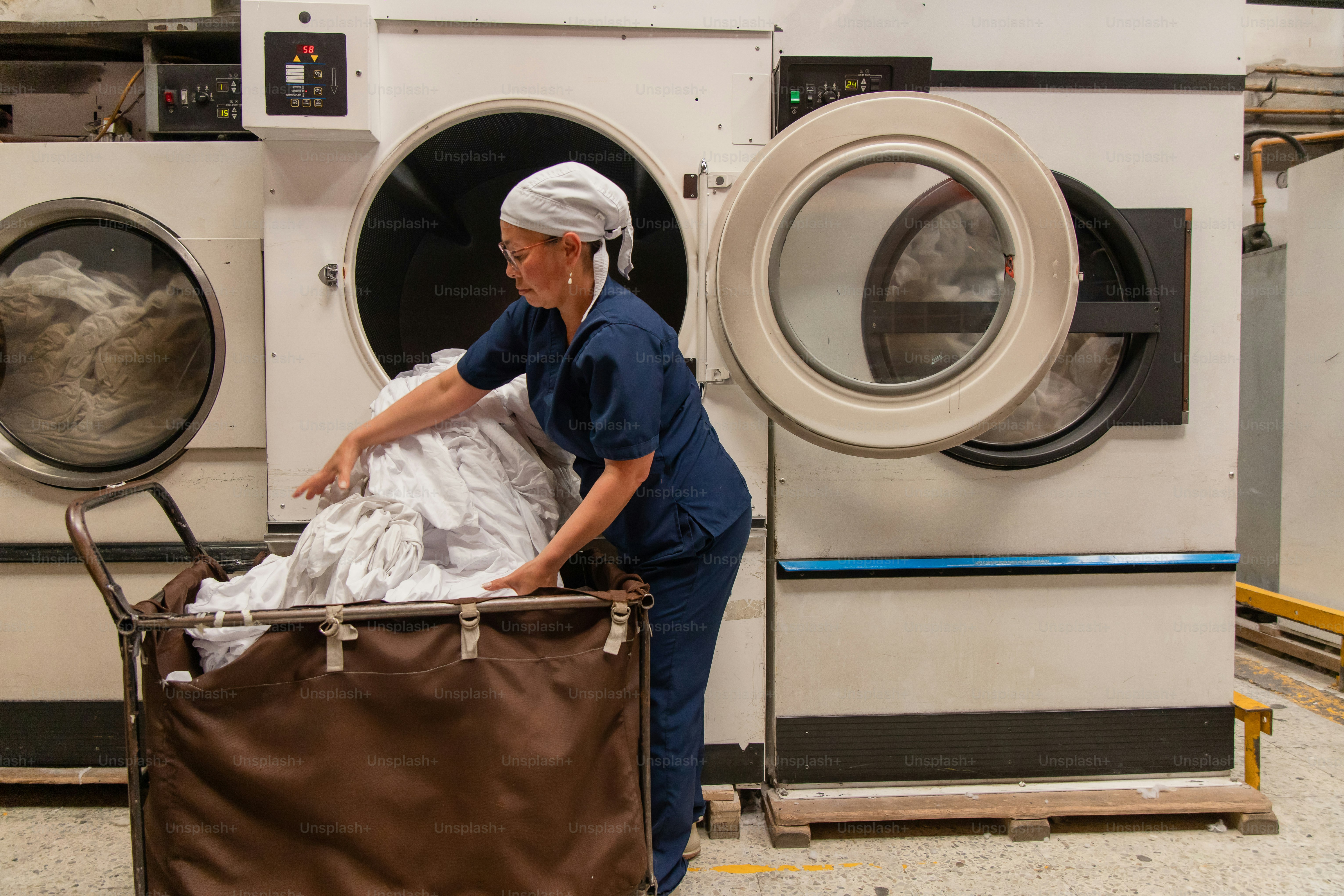 Woman loading laundry into a commercial dryer. photo – Laundry Image on ...
