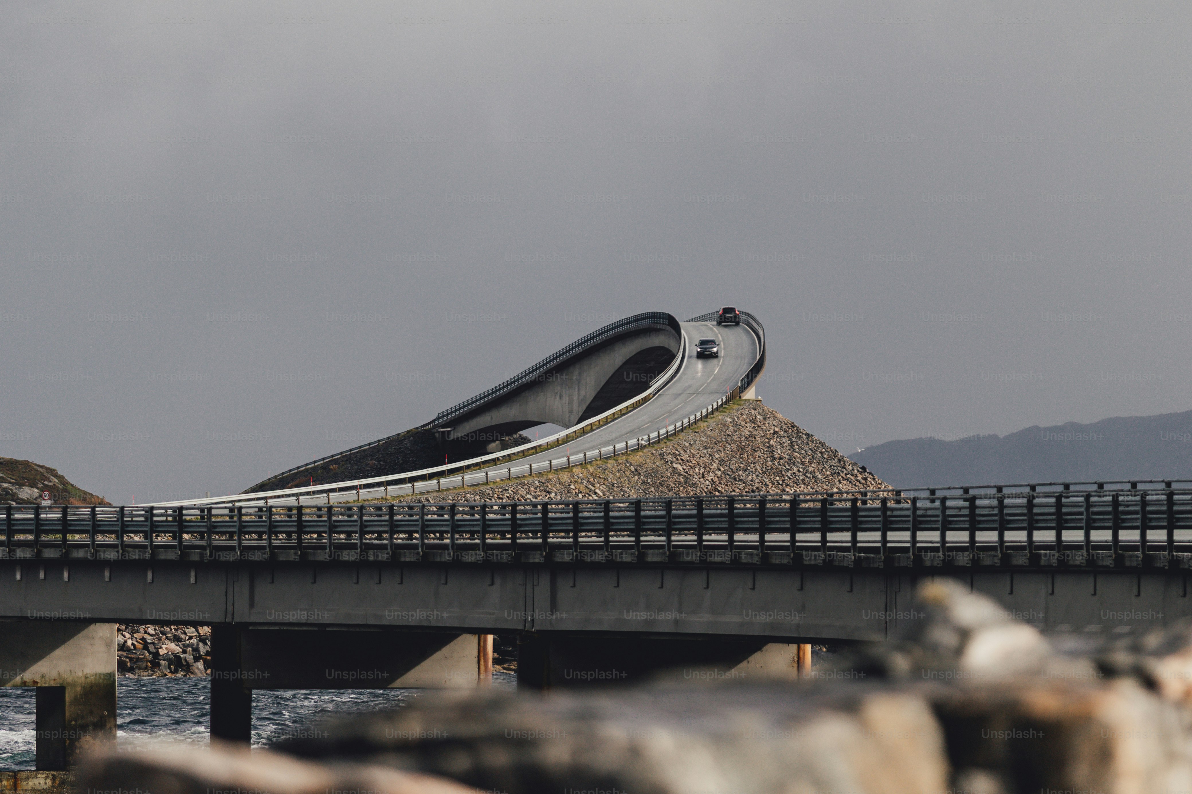 Modern bridge structure over water with rocky foreground photo – Car ...