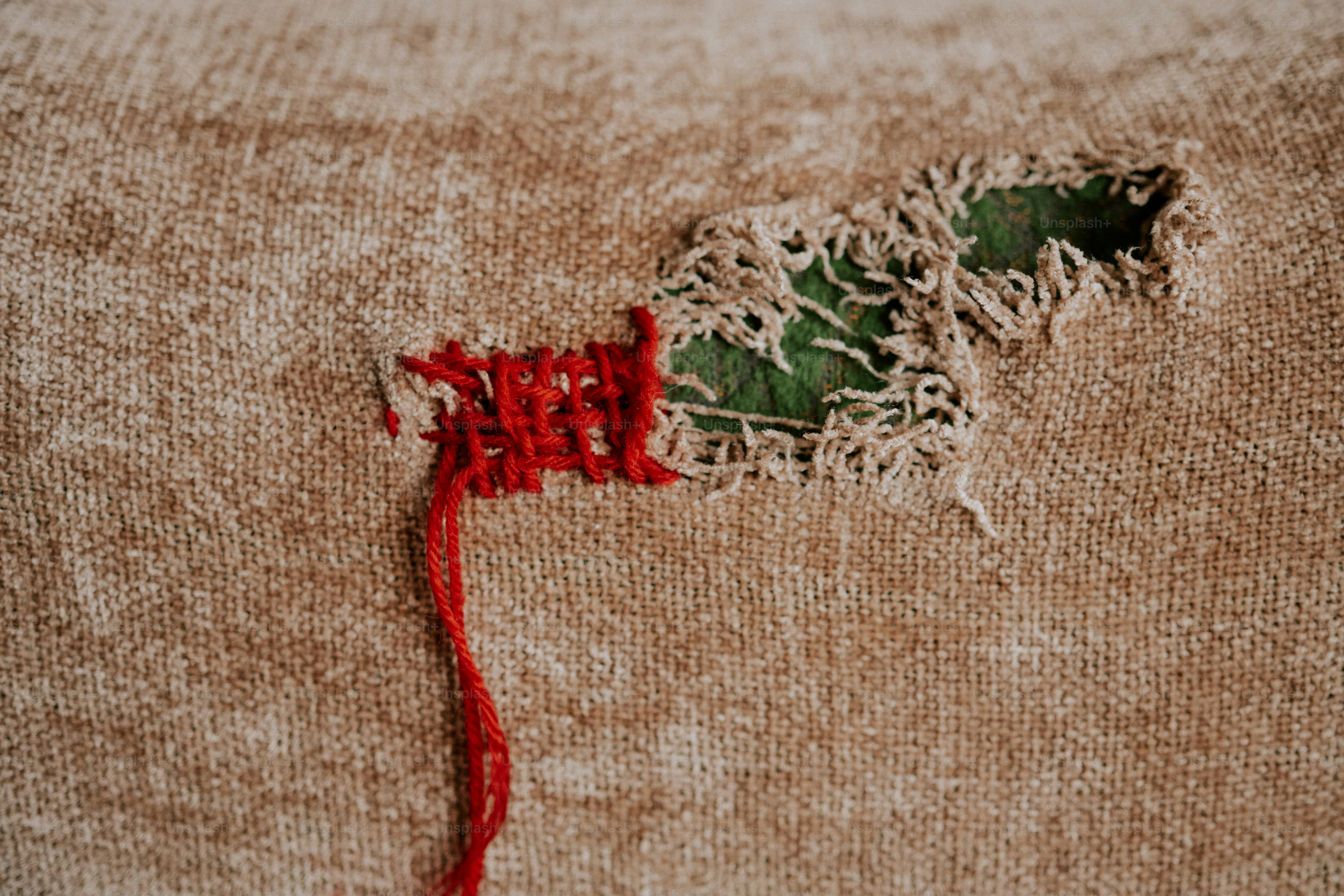 Red thread mending a torn fabric with green backing. photo – Repair ...