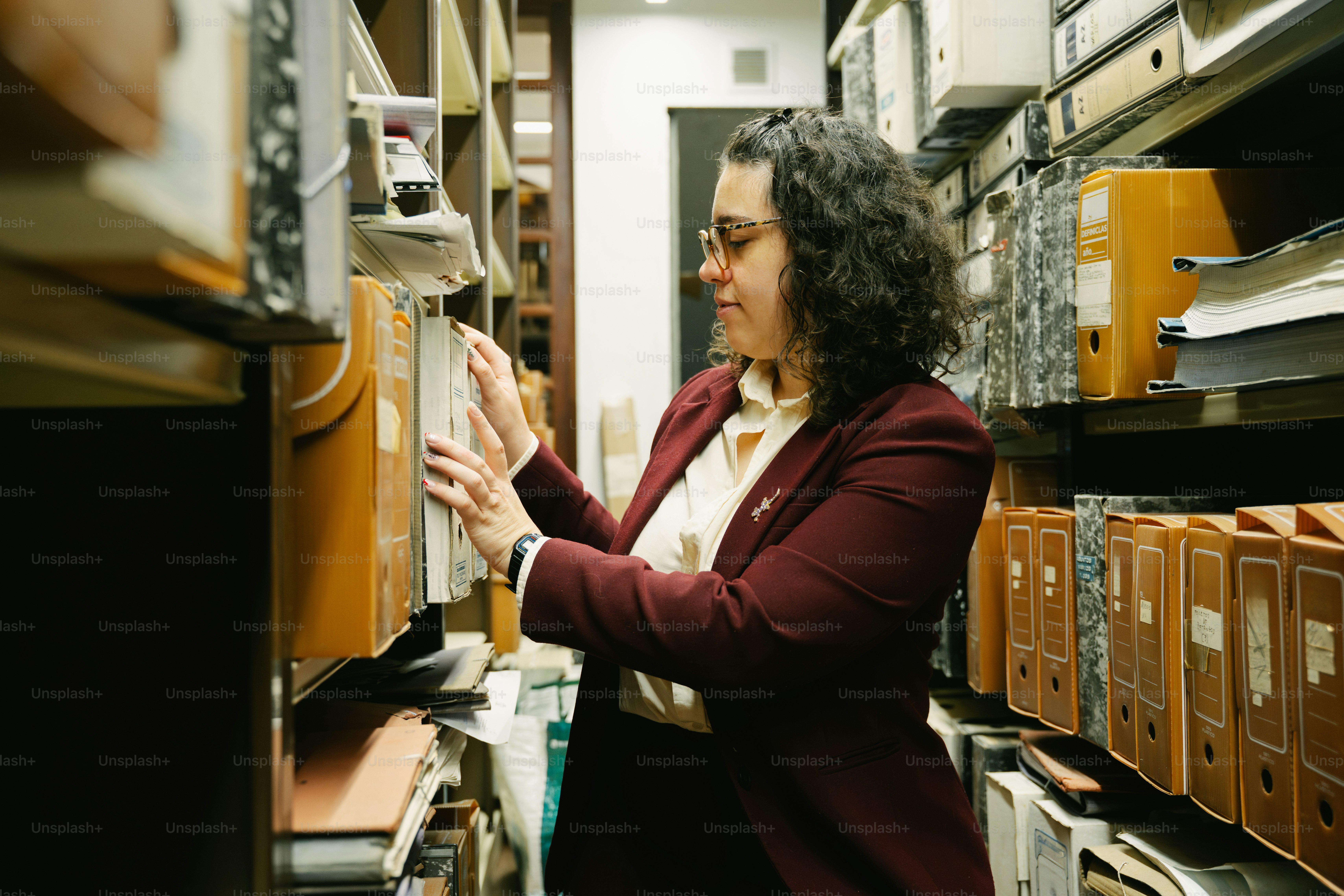 Mujer agachada entre las estanterías de la biblioteca mirando archivos ...