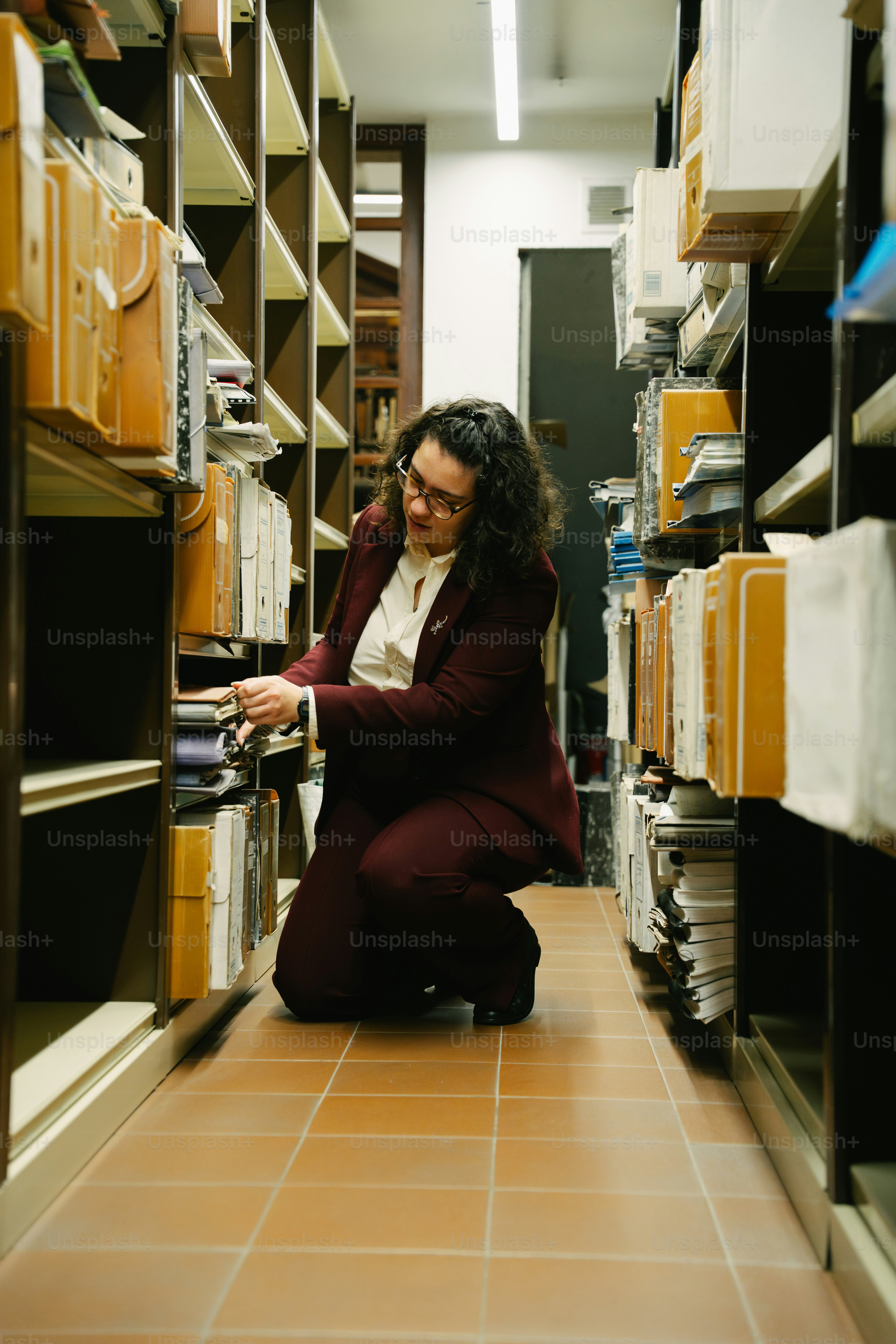 Mujer agachada entre las estanterías de la biblioteca mirando archivos ...