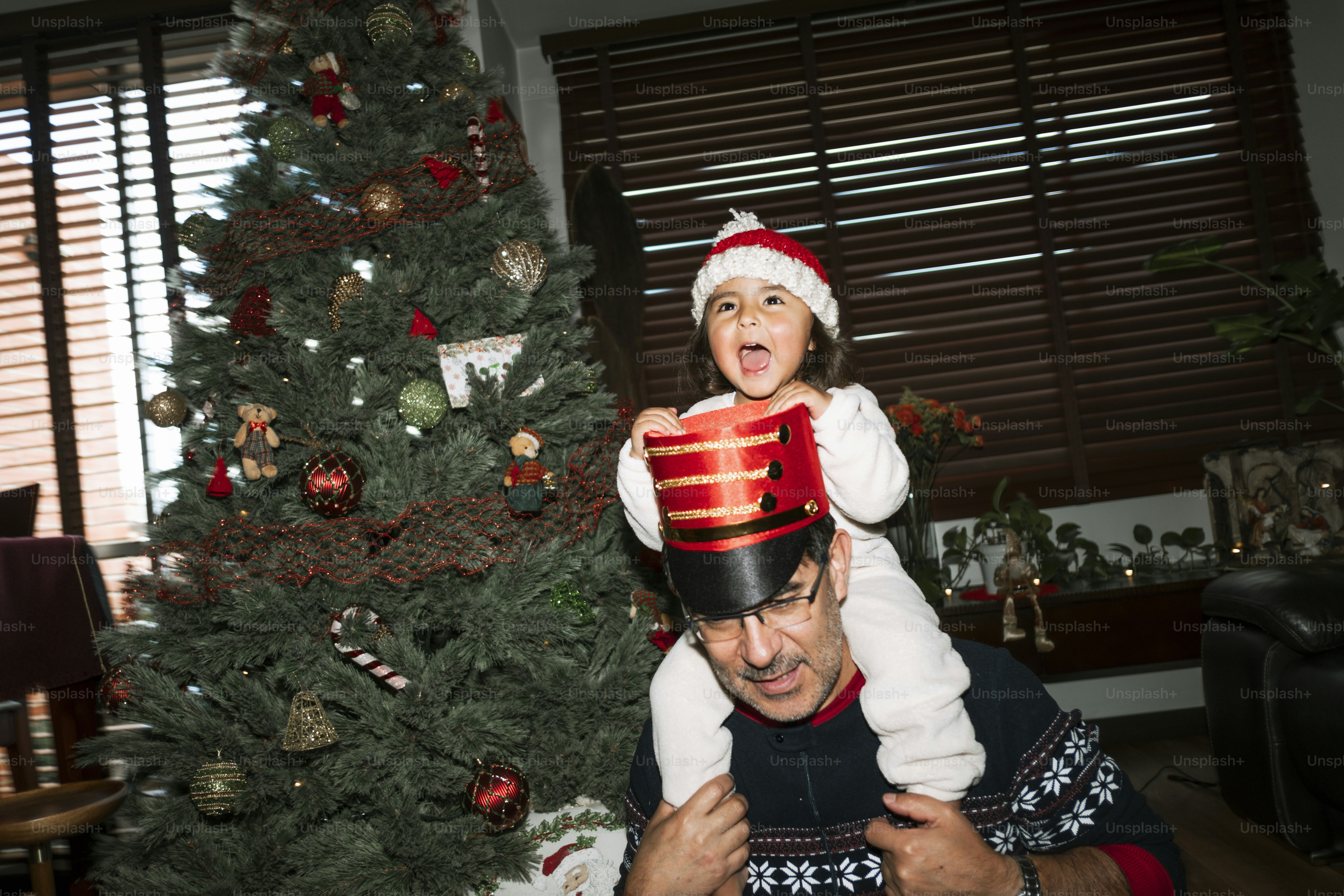 Father carries daughter wearing a nutcracker hat near christmas tree ...