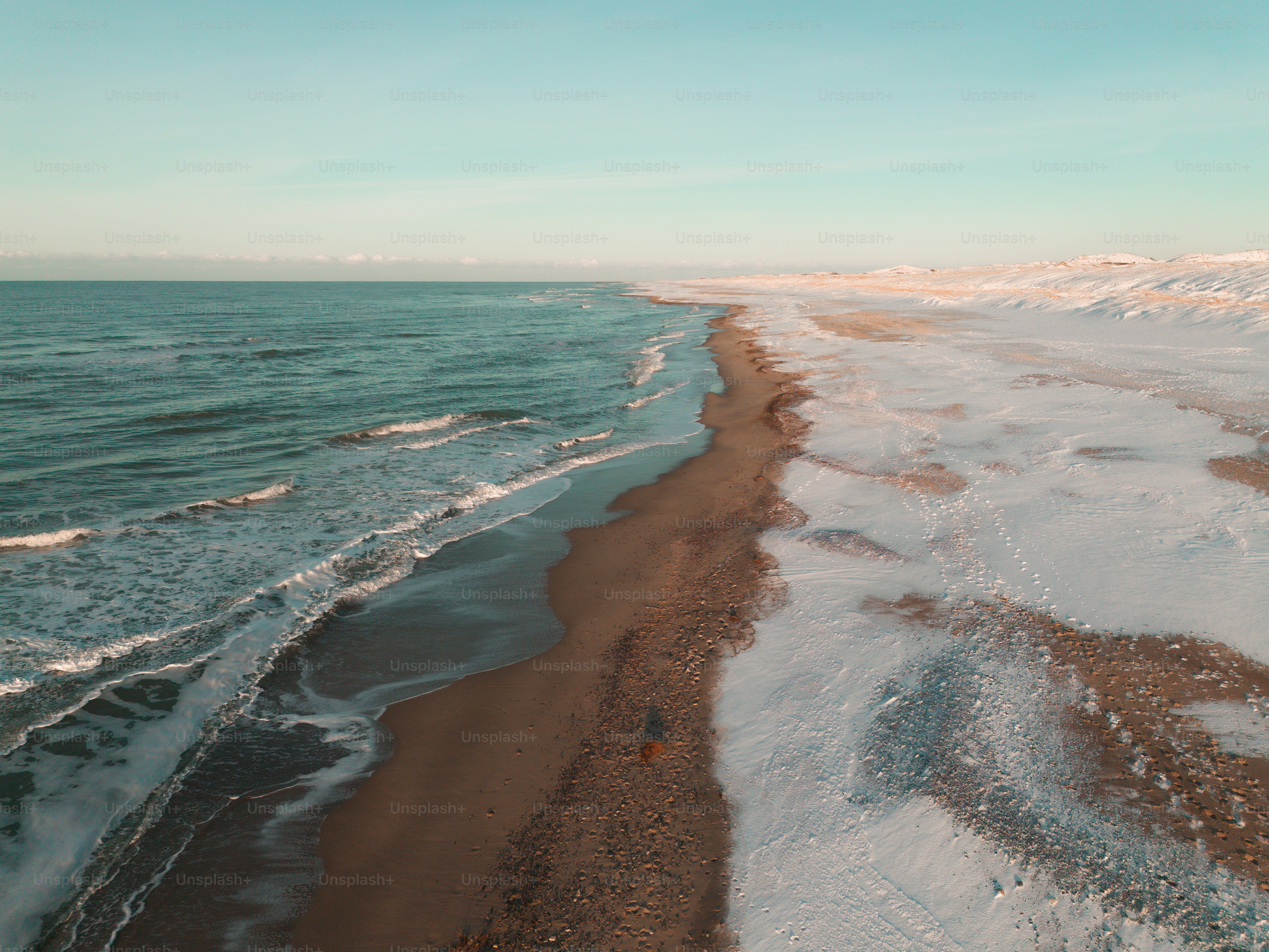Las olas del océano se encuentran con una playa nevada con montañas ...