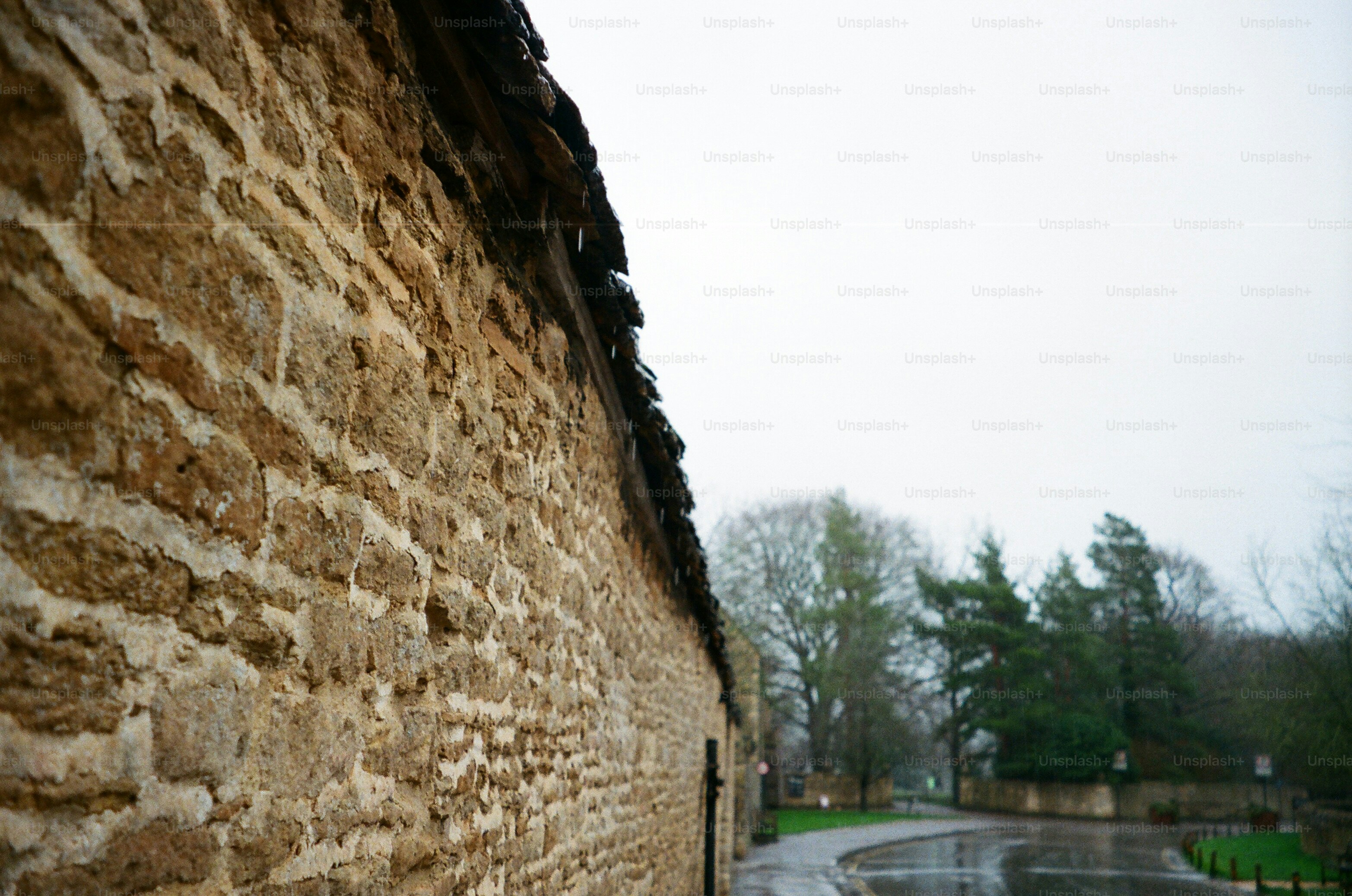 A stone wall runs alongside a wet road. photo – Film photography Image ...