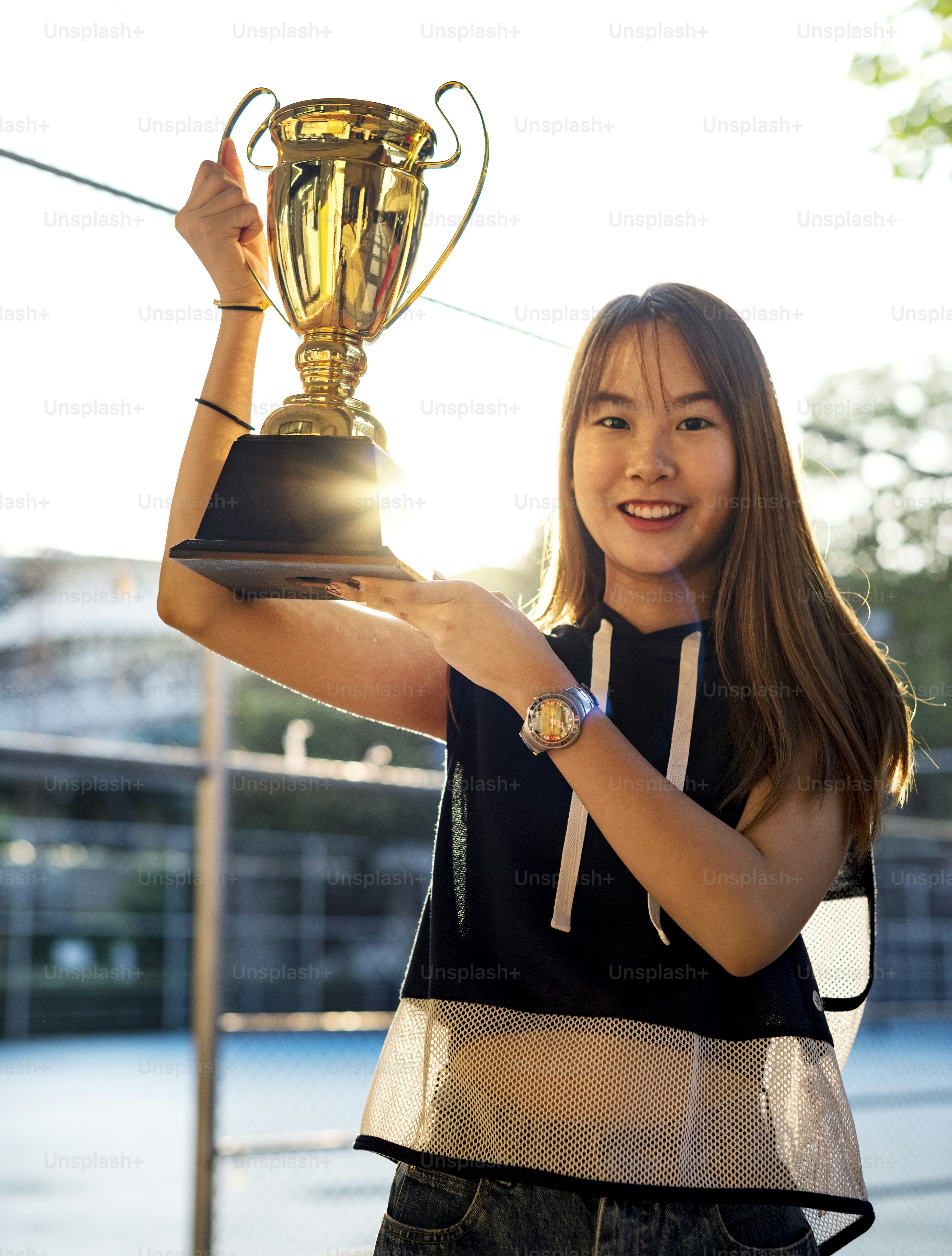 Asian teenage girl in sporty clothes holding up a trophy outdoors photo ...