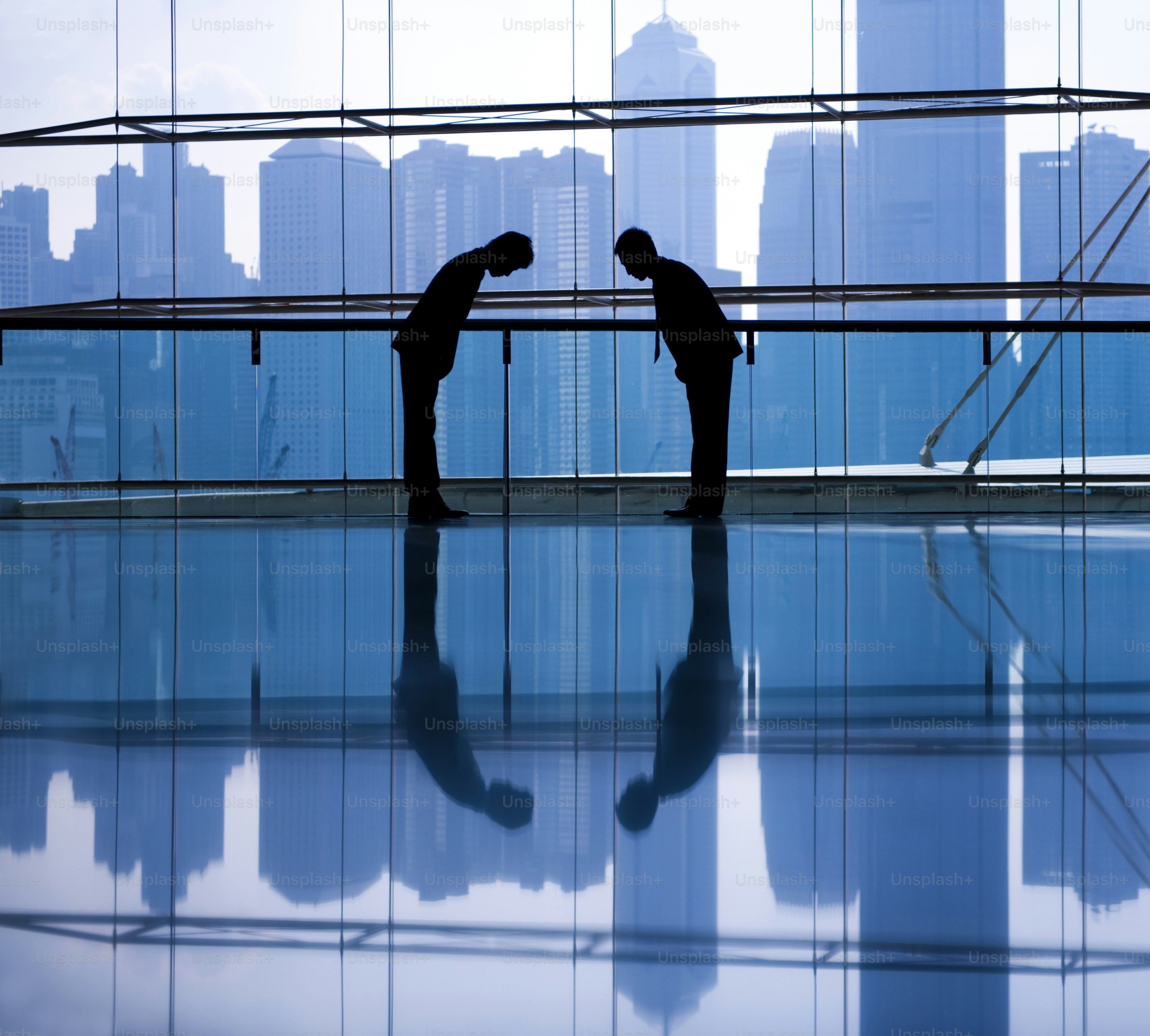 Two businessmen bowing to each other with city skyline reflection ...