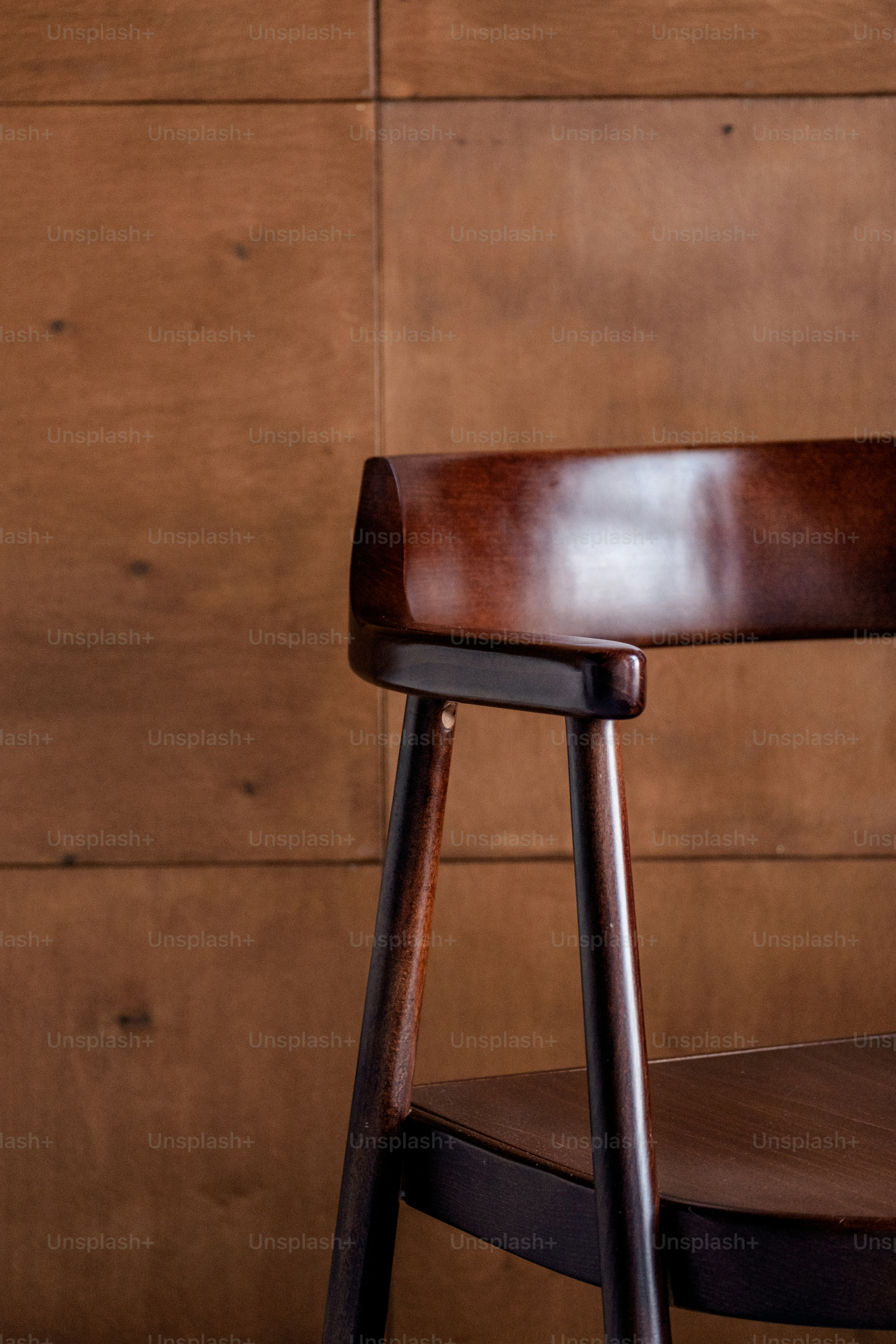A close-up of a wooden chair against a wood-paneled wall. photo ...