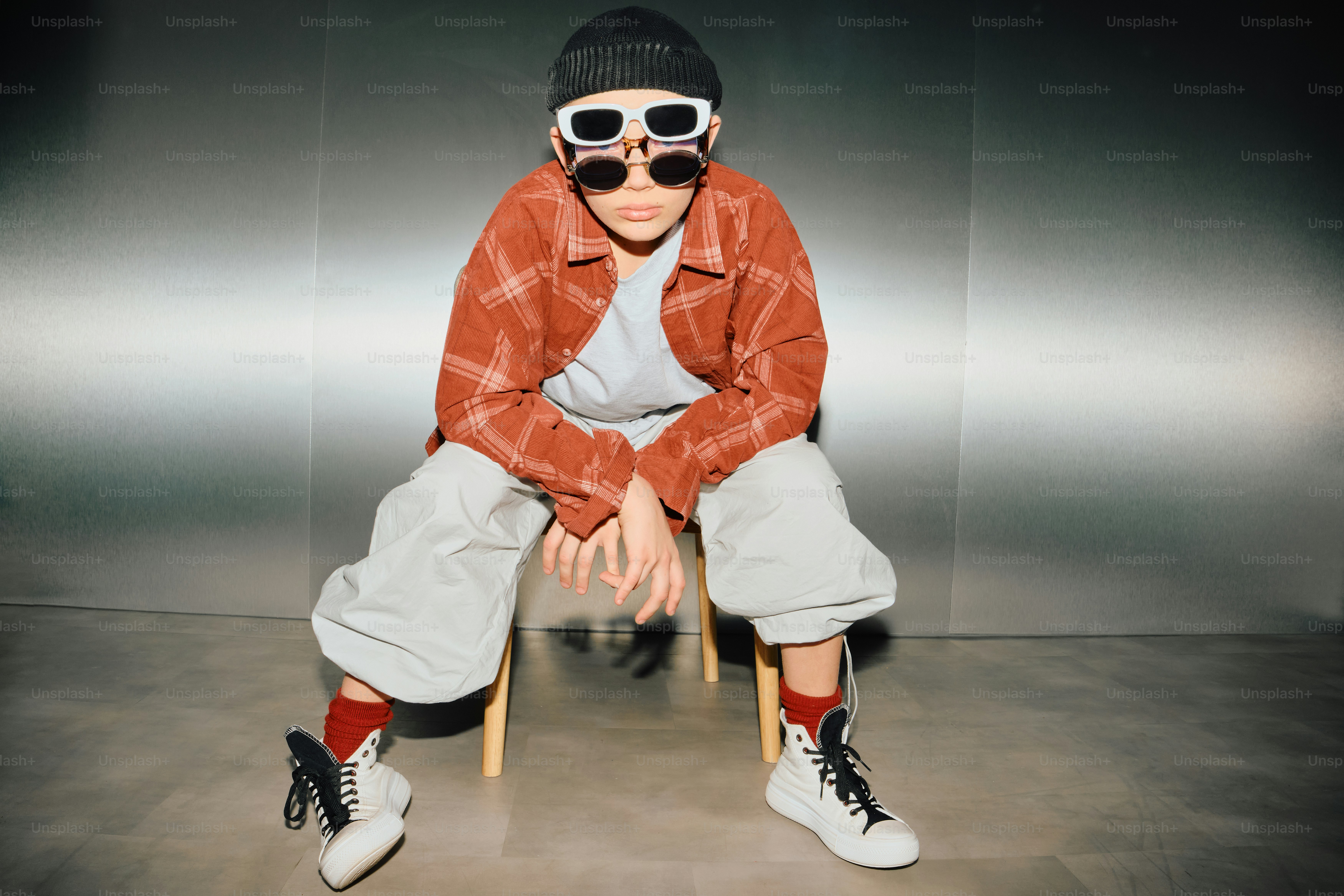 Person in stylish outfit sitting on chair against metallic background ...