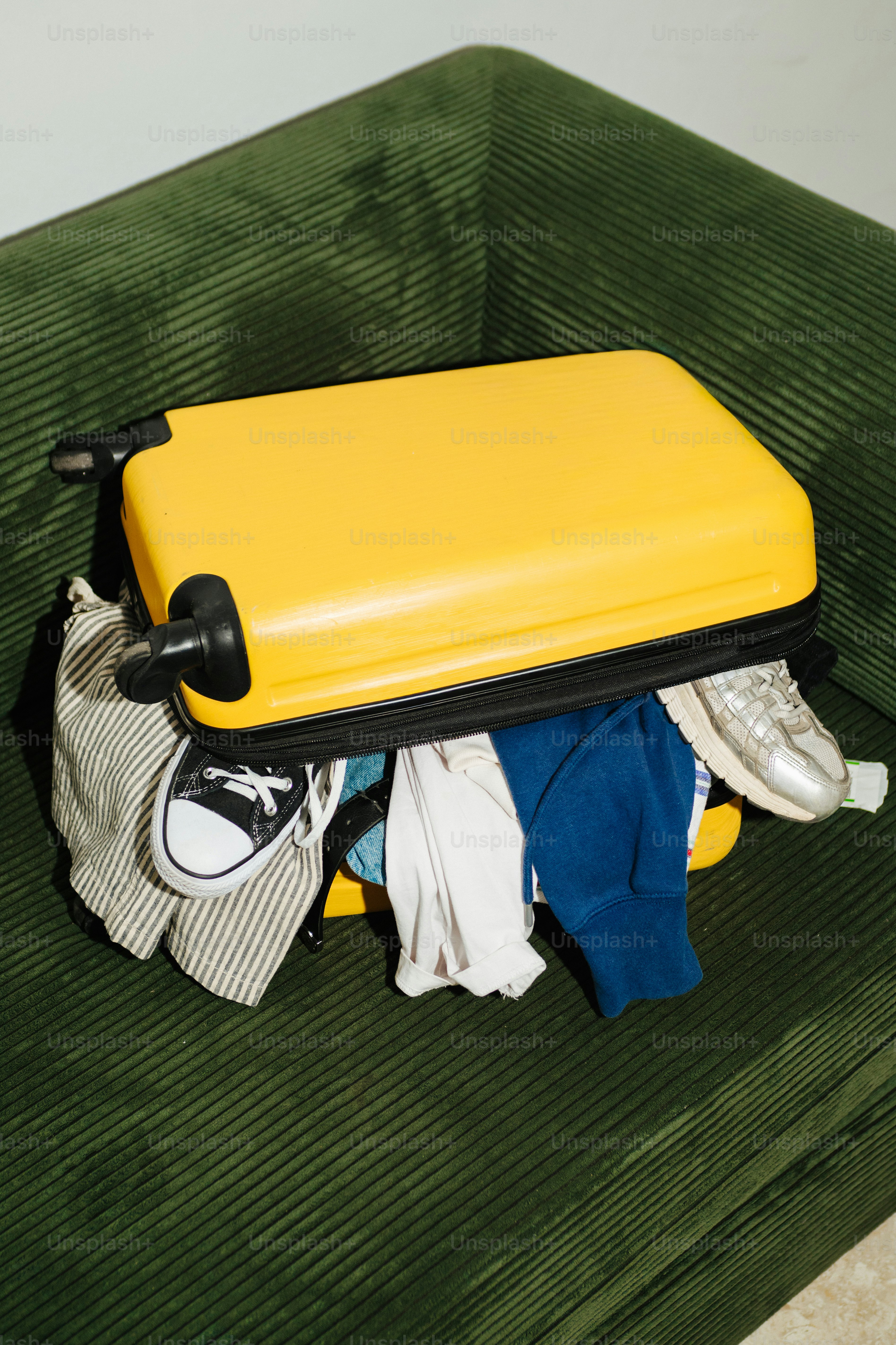 Yellow suitcase overflowing with clothes and shoes on green sofa. photo ...