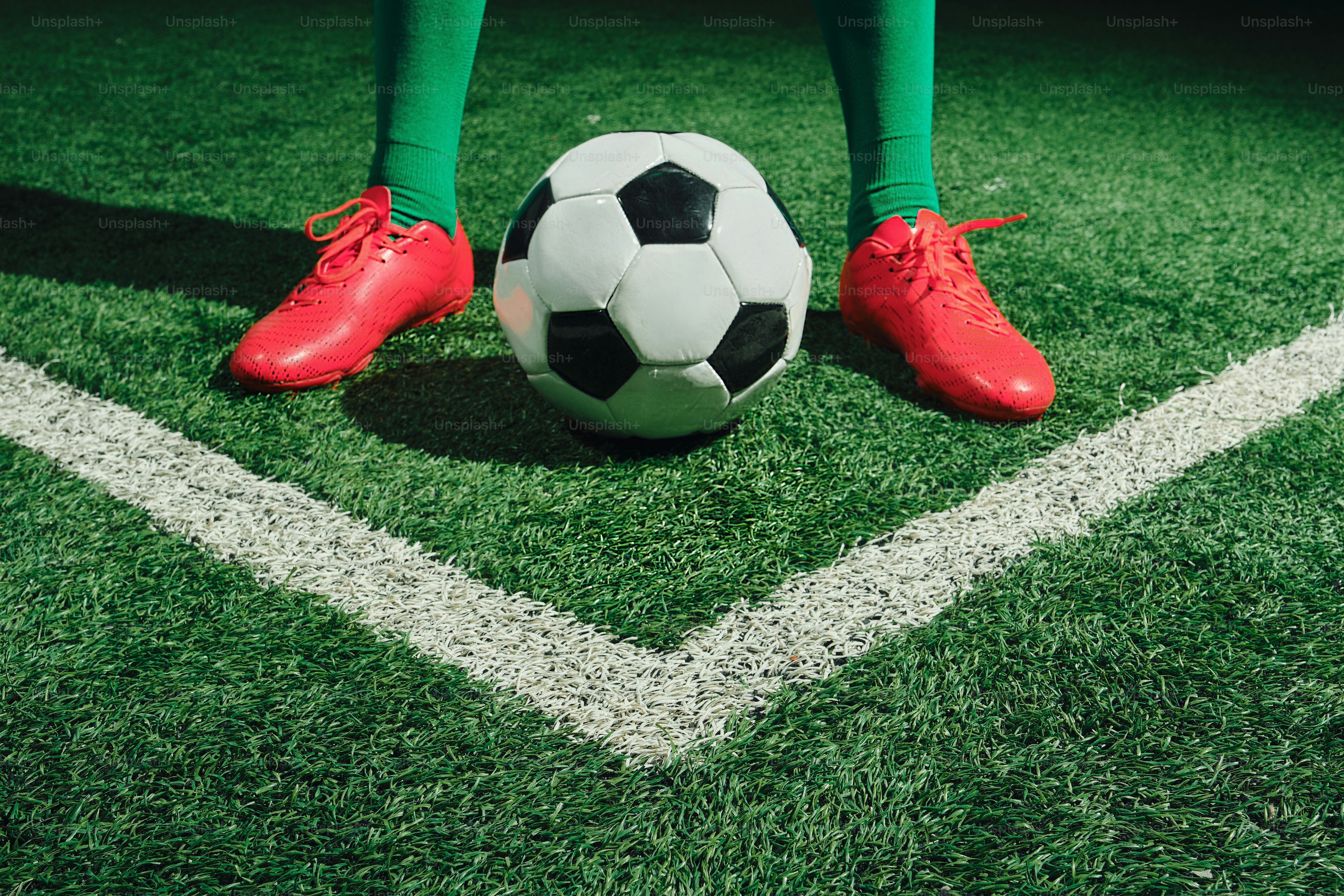 A soccer ball on a green field with red cleats. photo – Football Image ...