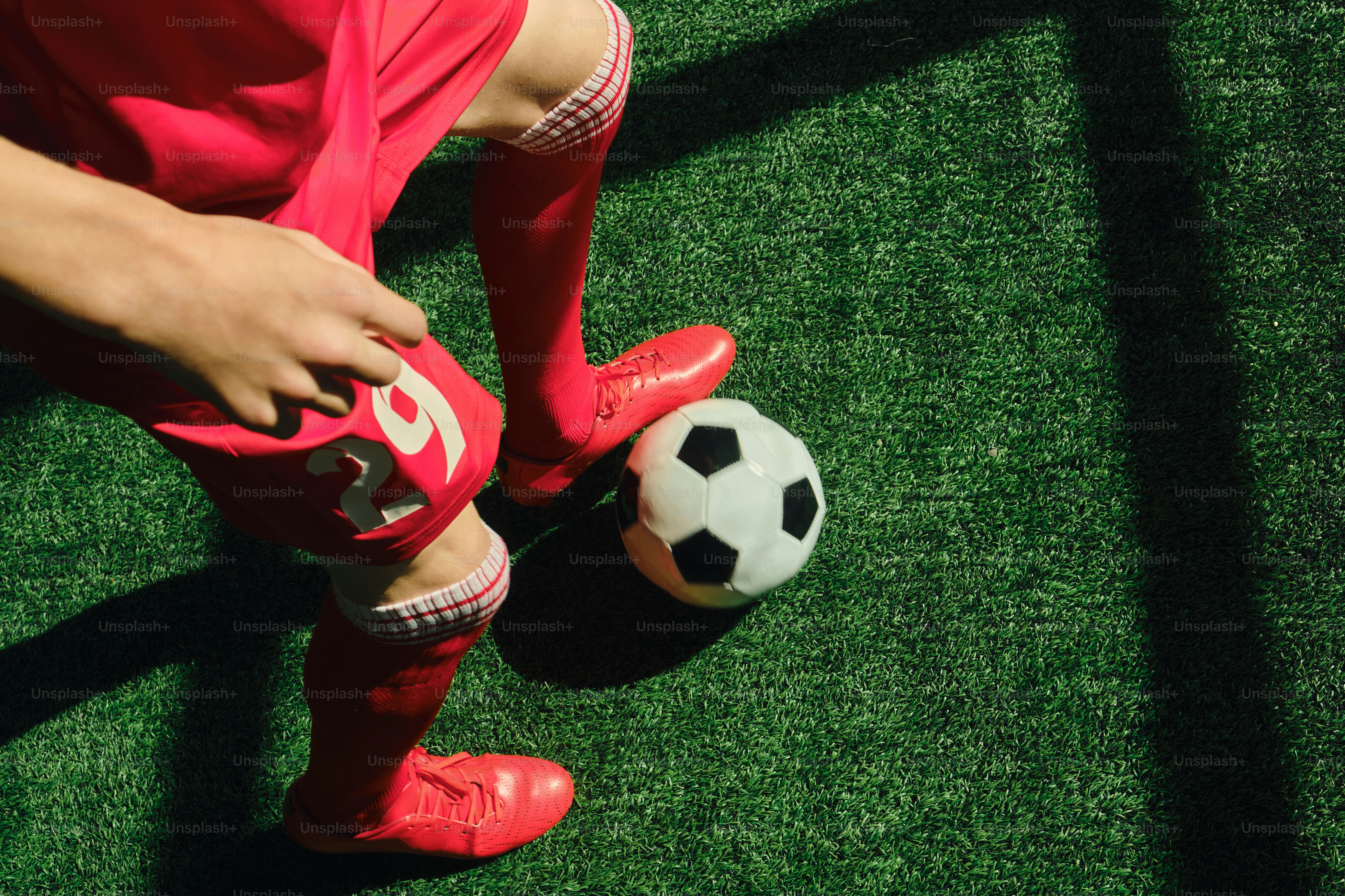 A soccer ball on a green field with red cleats. photo – Football Image ...